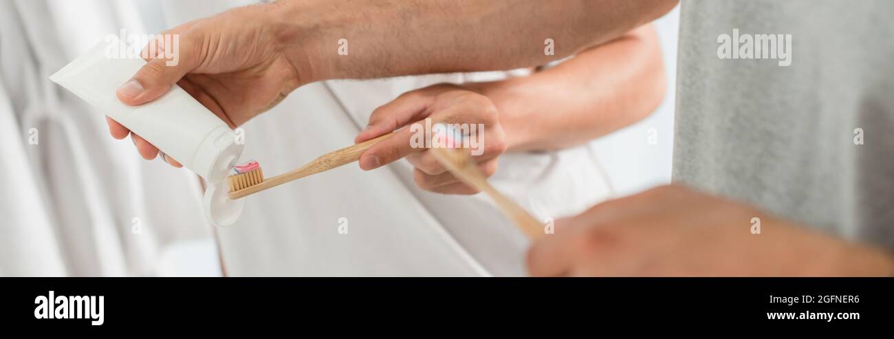 partial view of man squeezing toothpaste on toothbrush near boyfriend ...