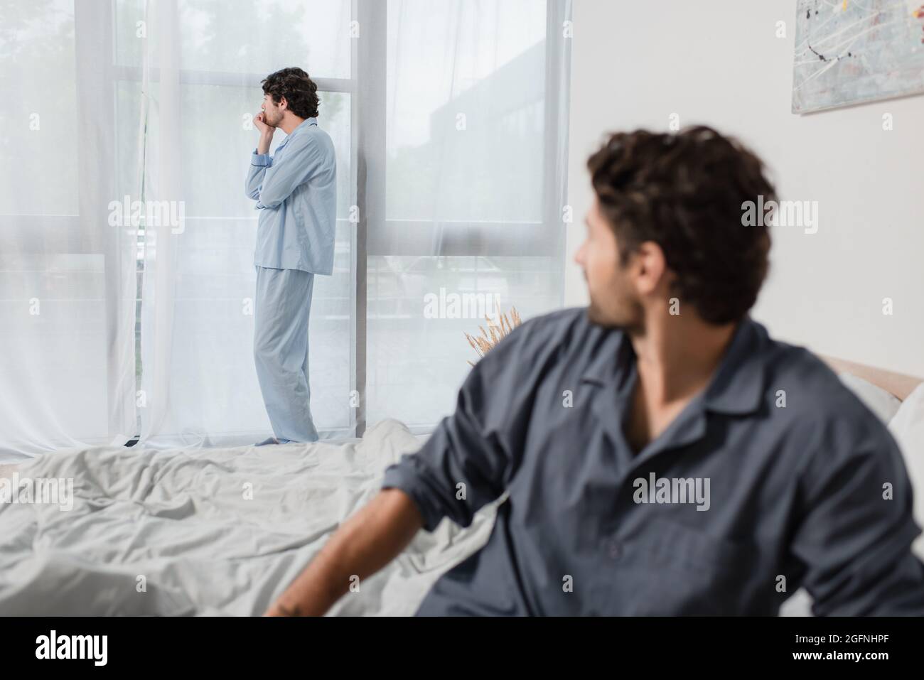 man standing and looking at window with blurred boyfriend on foreground ...