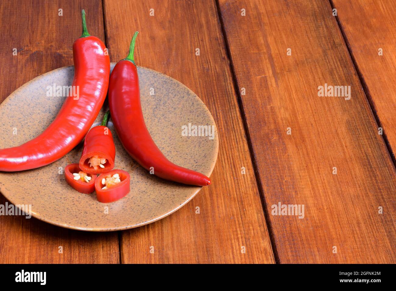 Two red pods of chili pepper and their slices lie on a brown ceramic ...