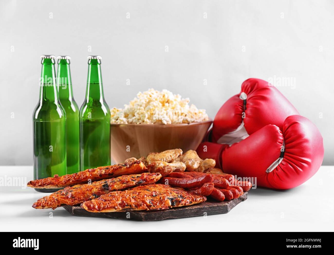 Boxing gloves, snacks and bottles of beer on table against light ...