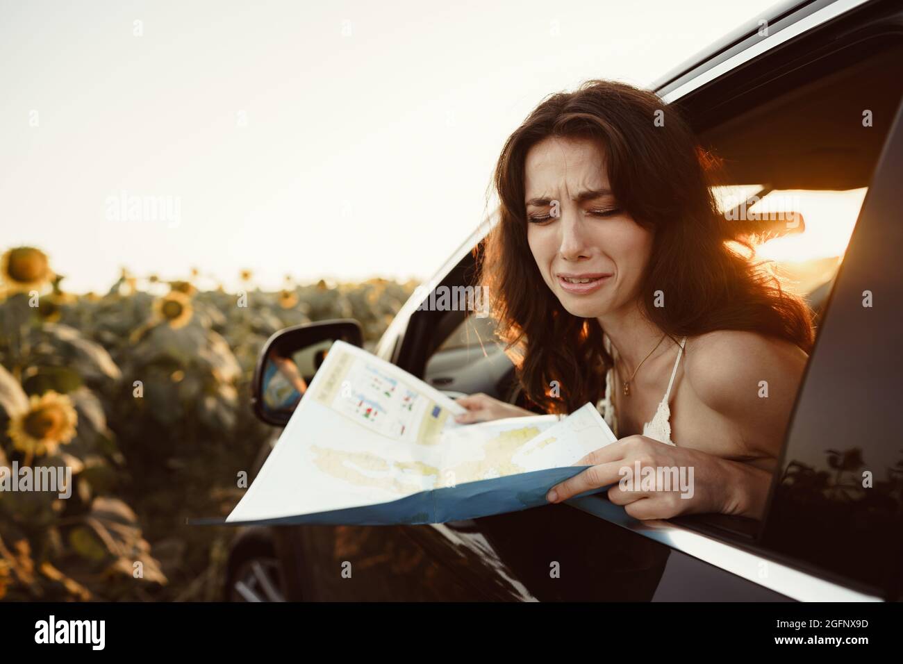 Lost young woman sitting in her car in the countryside and looking at ...