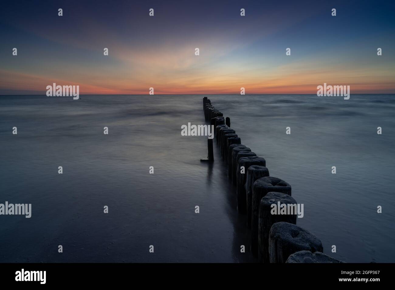 long exposure view of an ocean sunset with sandy beach and wooden pylon ...