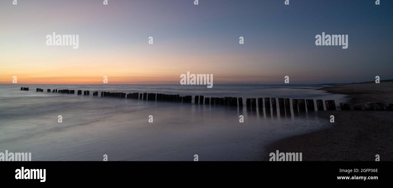 long exposure view of an ocean sunset with sandy beach and wooden pylon ...