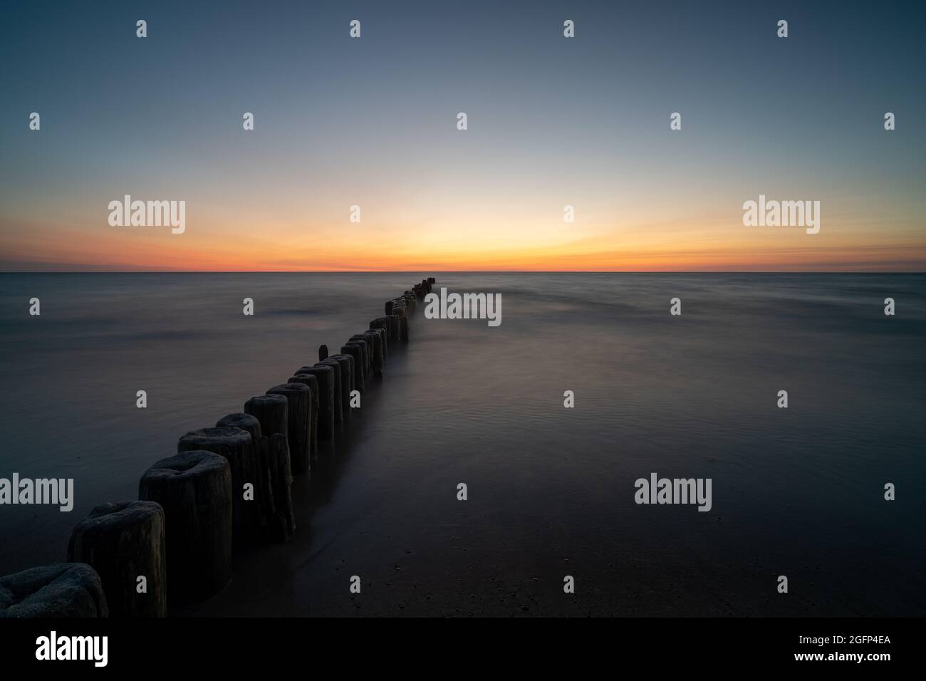 long exposure view of an ocean sunset with sandy beach and wooden pylon ...