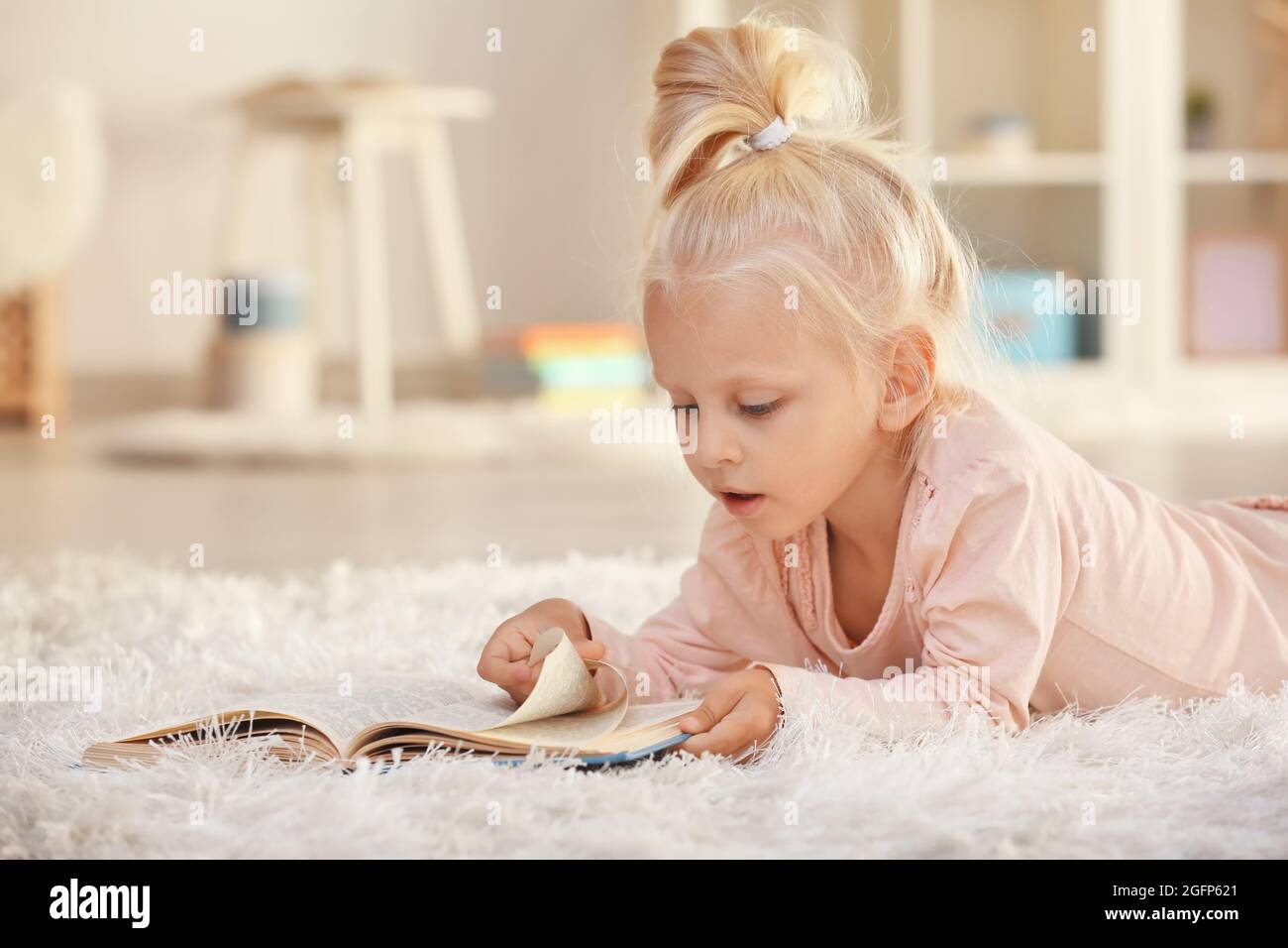 Small girl reading book on carpet Stock Photo - Alamy