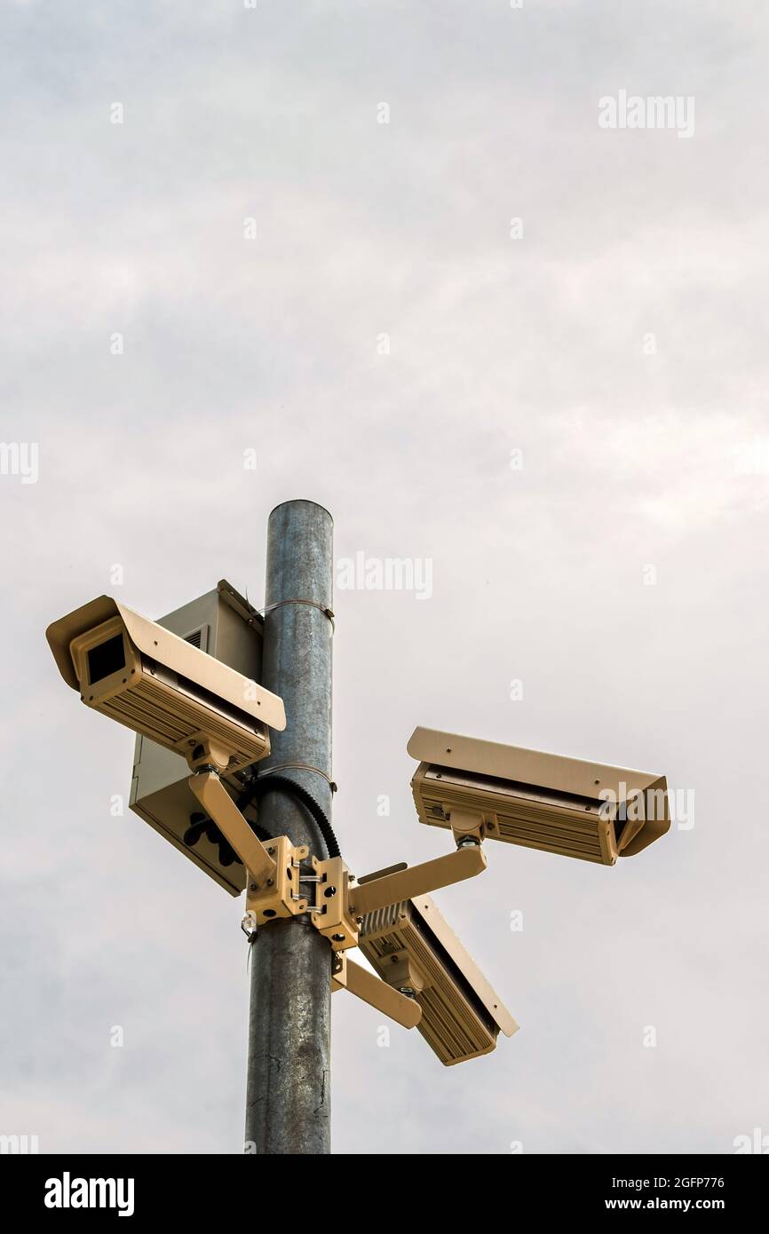 Vertical shot of three surveillance cameras on a gray cloudy sky ...