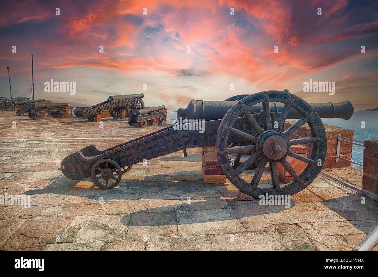 Cannons of artillery standing on a stone platform by the sea at sunset ...