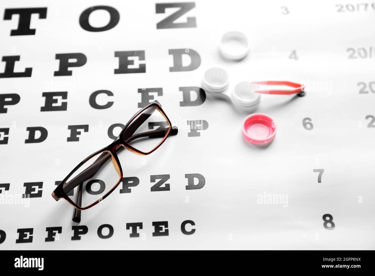 Glasses, lenses container and pincer on eye test chart, close up view ...
