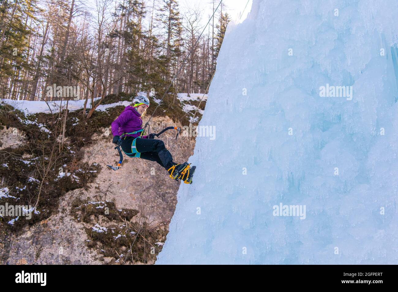 Female ice climber going down an ice waterfall, using a safety top rope ...