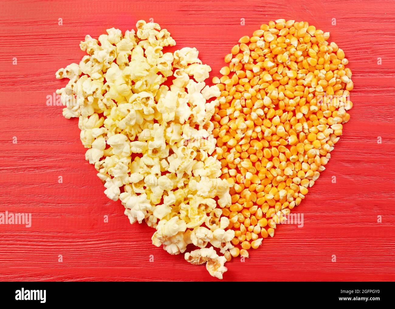 Heart made of popcorn and maize grains on red wooden background, top ...