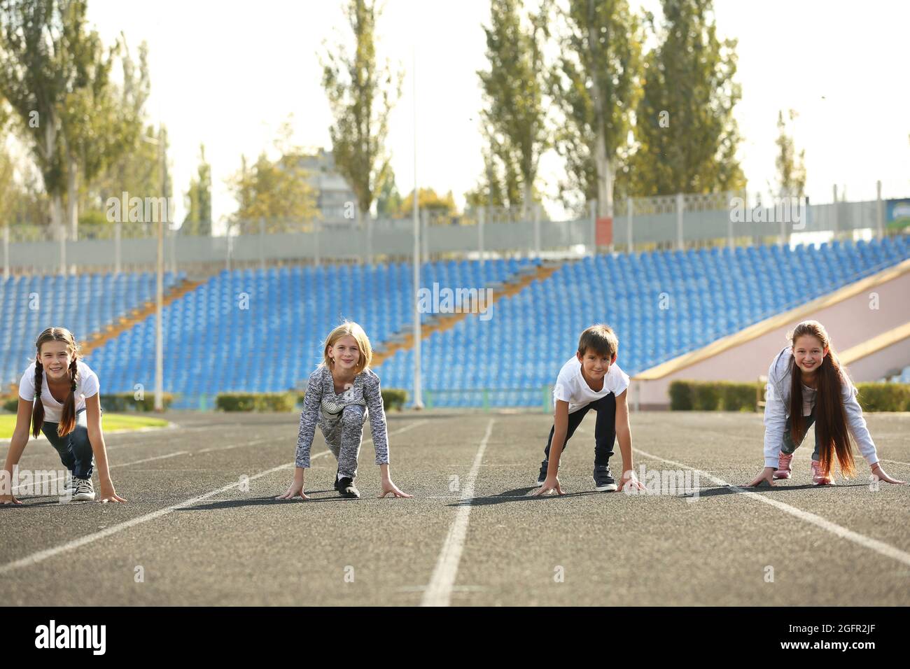 Cheerful children in ready position to run on track Stock Photo - Alamy