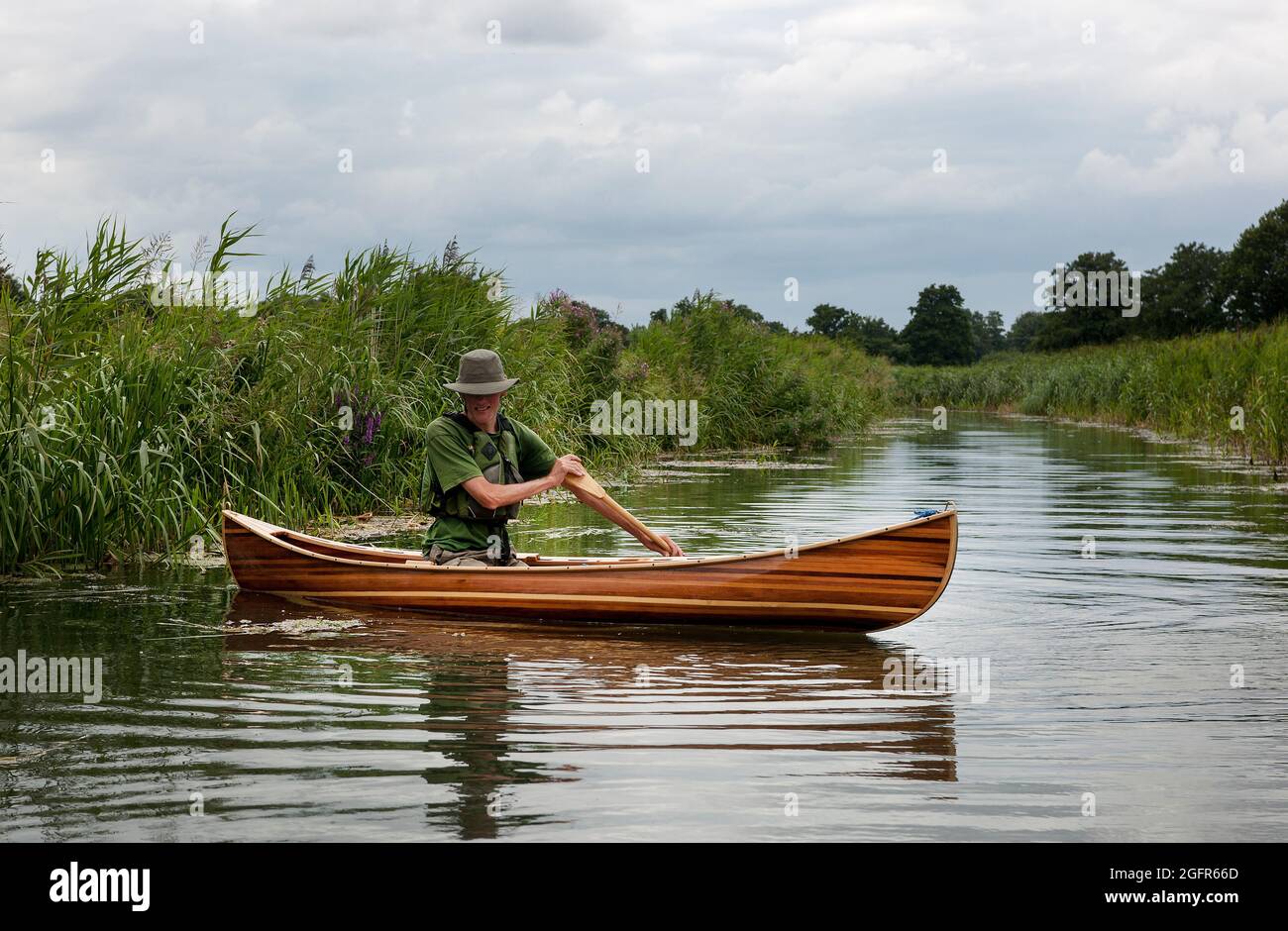 Man paddles a wooden Canadian Cedar Strip Canoe down a still river in ...