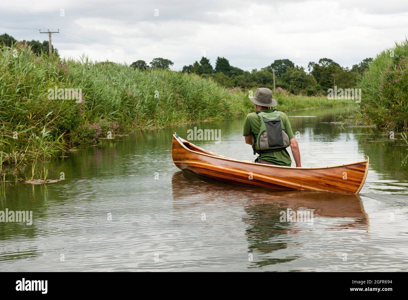 Man paddles a wooden Canadian Cedar Strip Canoe down a still river in ...