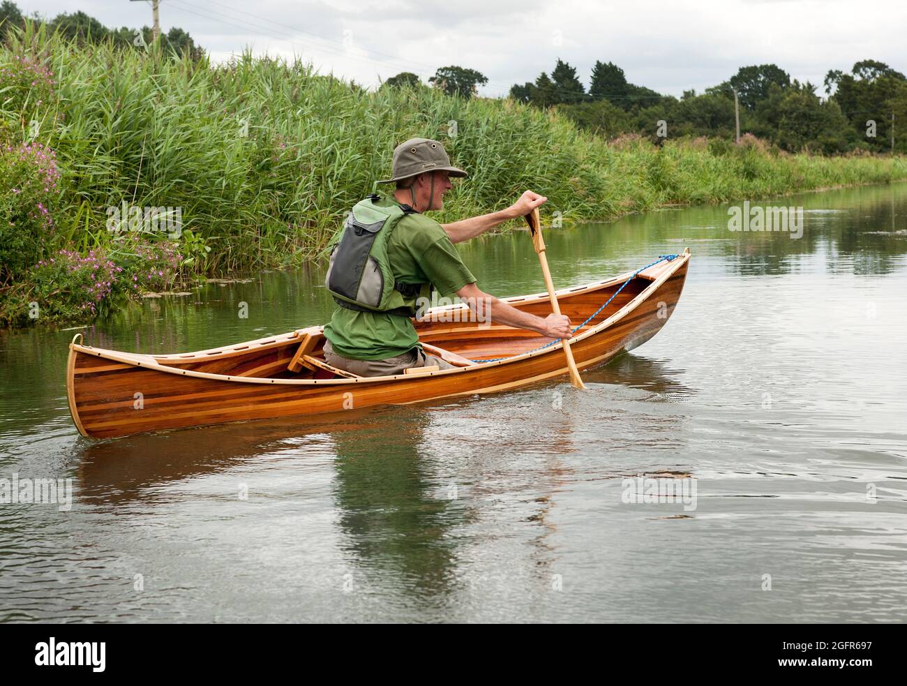 Man paddles a wooden Canadian Cedar Strip Canoe down a still river in ...
