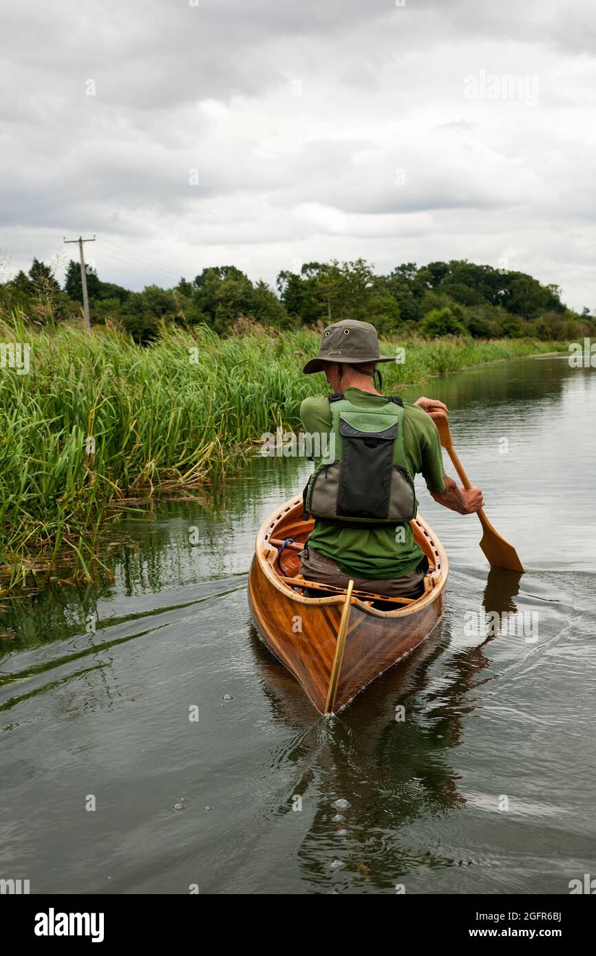 Man paddles a wooden Canadian Cedar Strip Canoe down a still river in ...