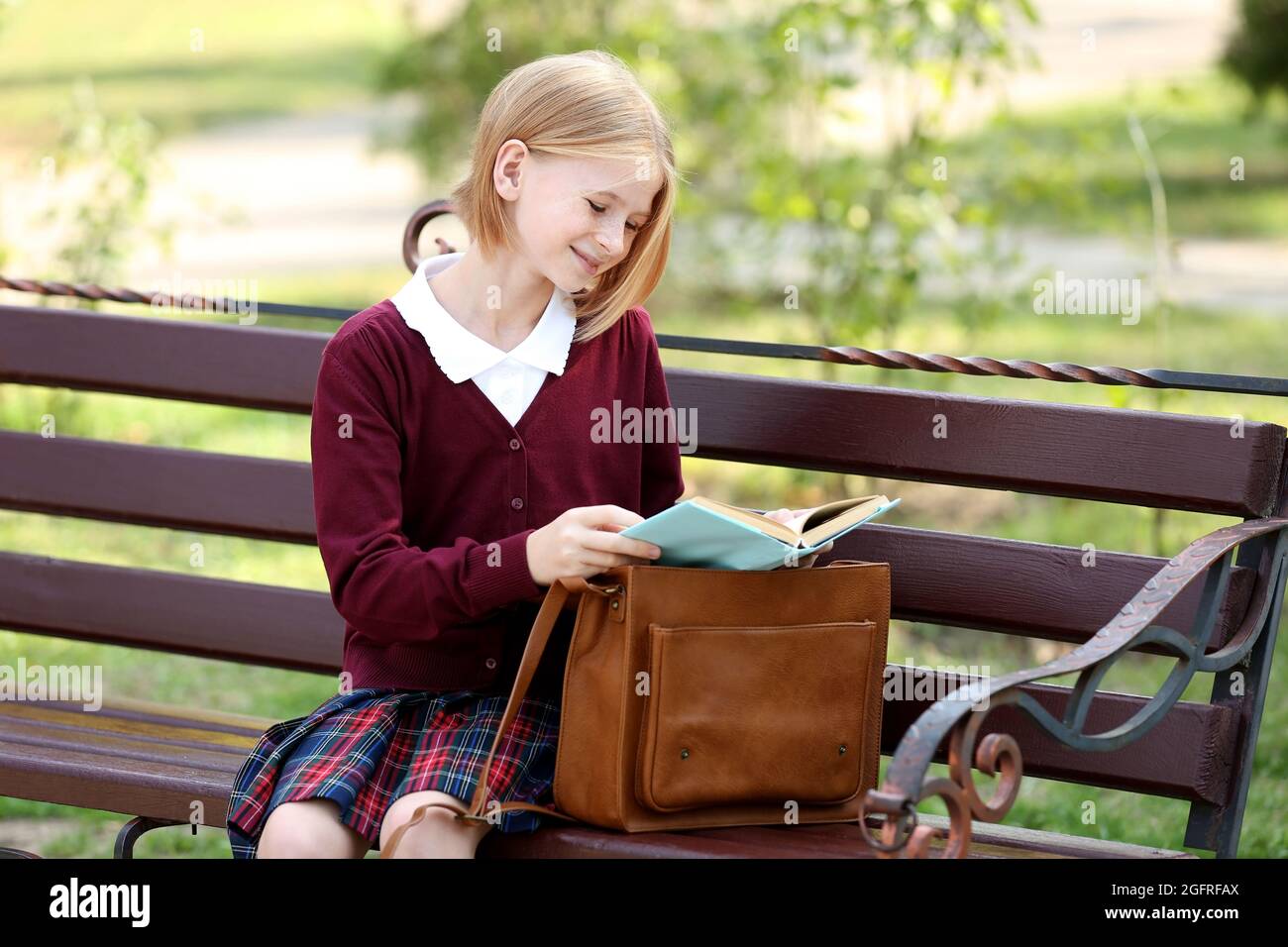 Schoolgirl reading book while sitting on bench in park Stock Photo - Alamy