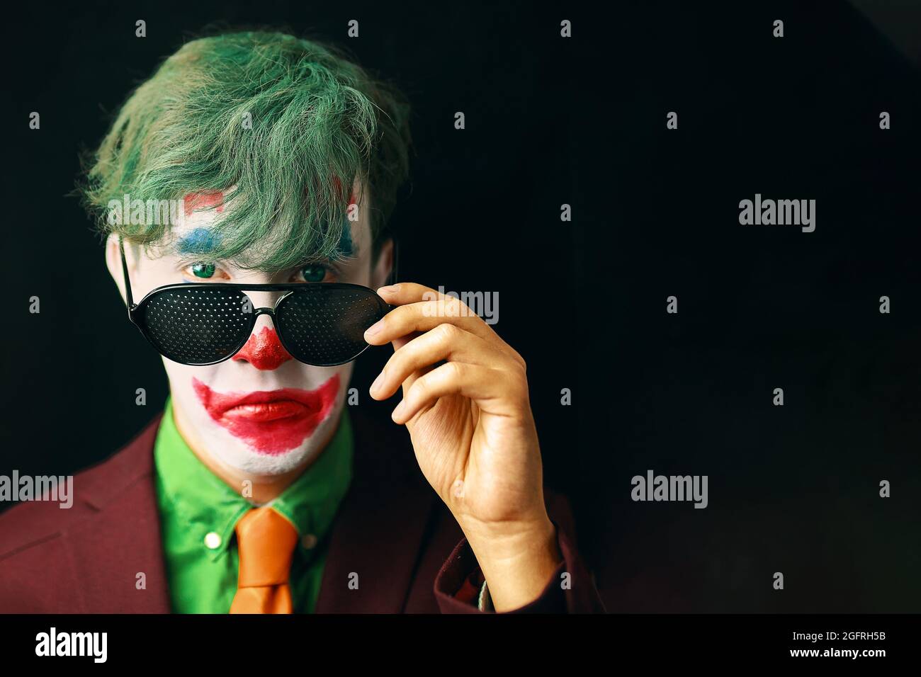 Man in mime makeup cosplay with green hair and a red suit an orange tie ...