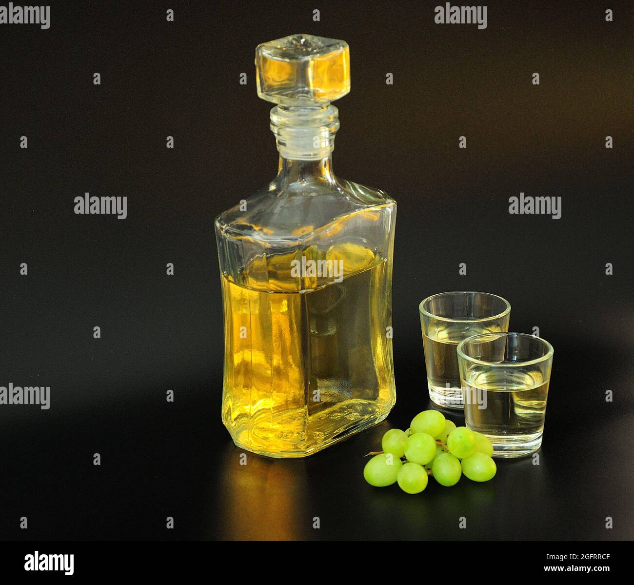 Grappa of white grapes in glasses and a glass bottle, next to a bunch ...