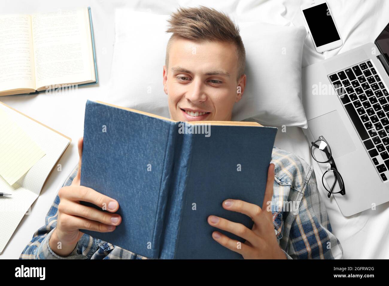 Handsome young man reading book while lying on bed Stock Photo - Alamy