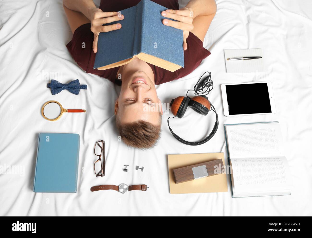 Young man lying on bed with different items Stock Photo - Alamy