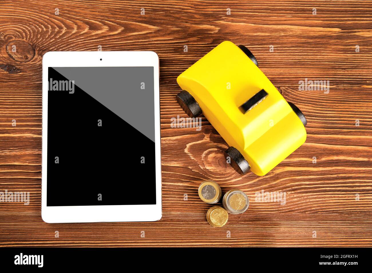 Yellow toy taxi cab, tablet and coins on wooden background Stock Photo ...