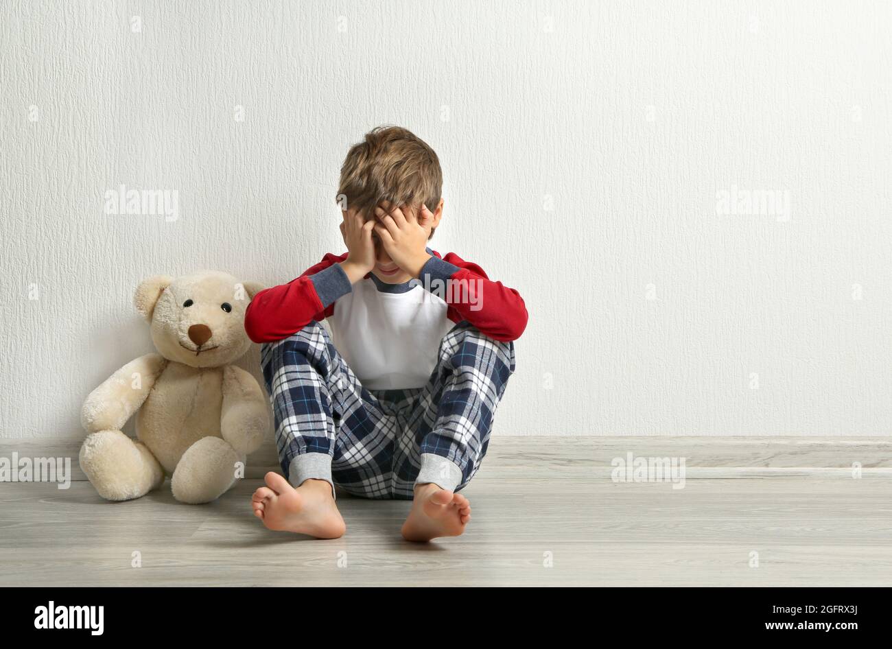 Crying little boy with teddy bear on floor in empty room Stock Photo ...