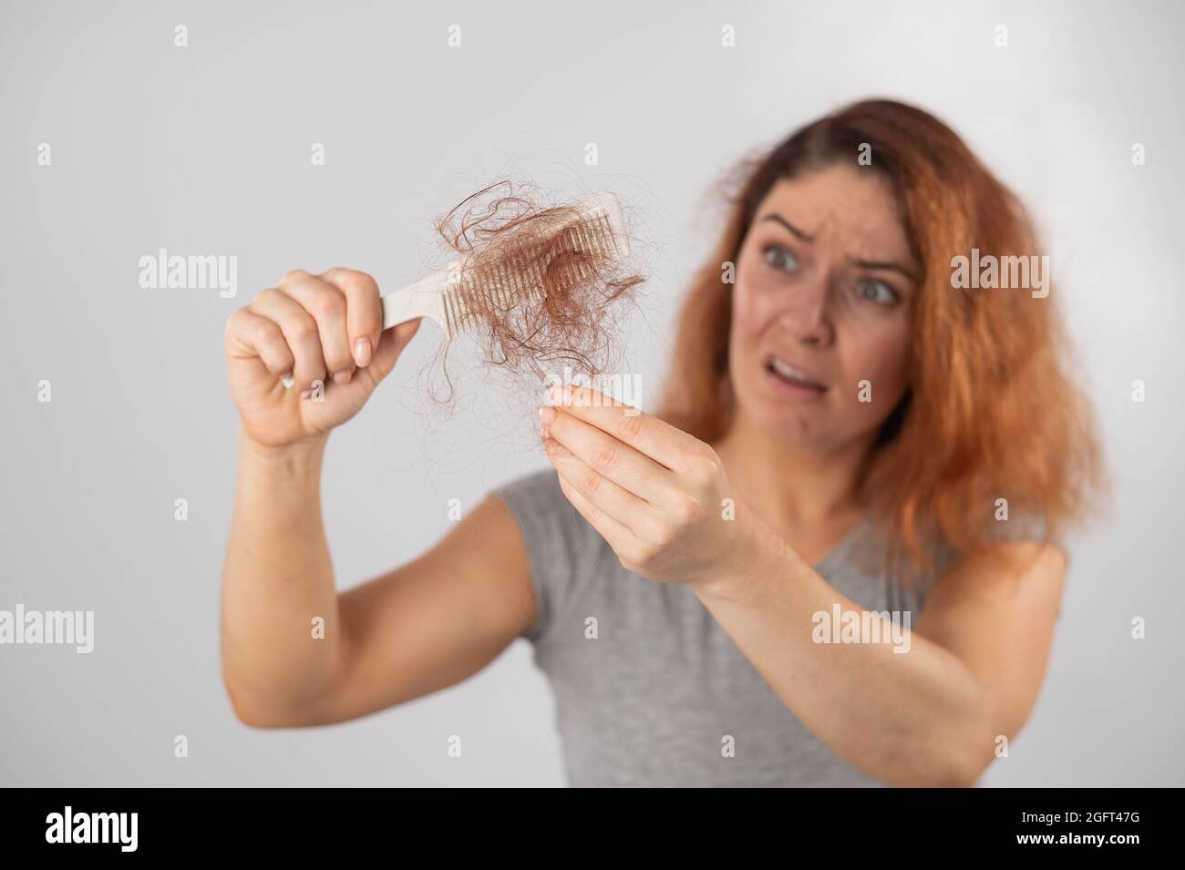 Caucasian woman with a grimace of horror holds a comb with a bun of ...