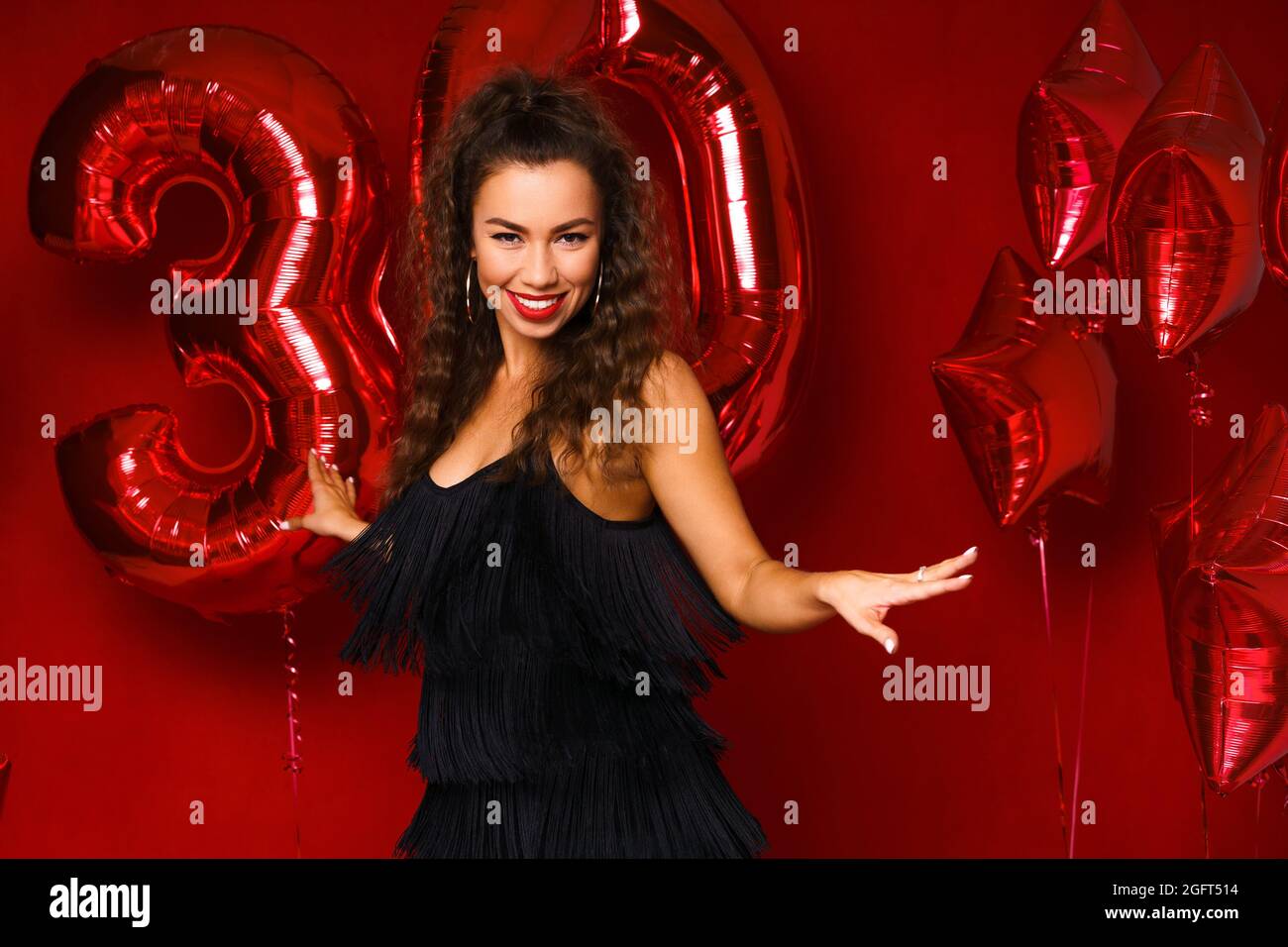 Portrait of happy 30 year old woman on red background with red balloons ...