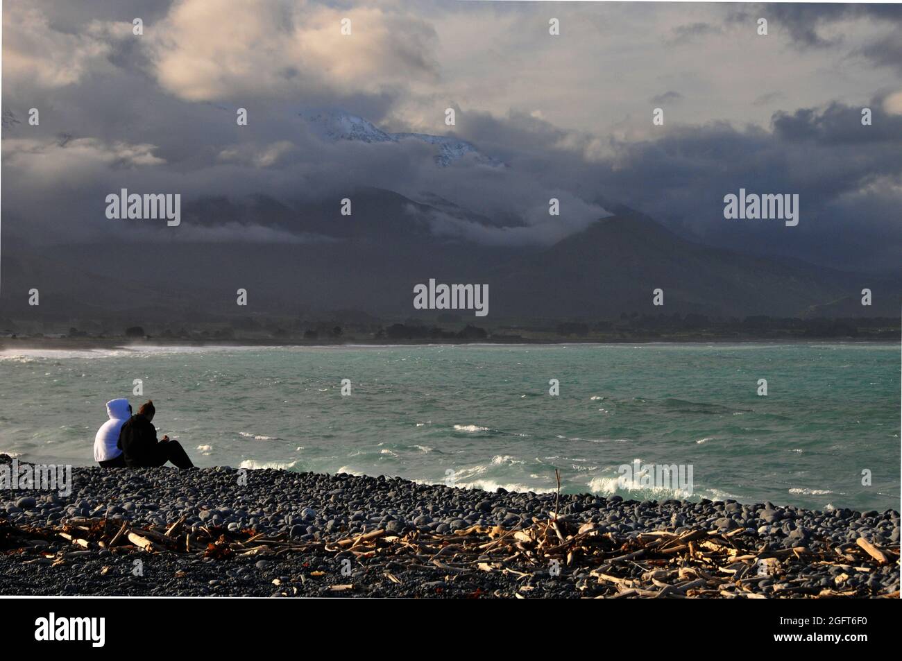 Two teenagers huddle on the rocky beach at Kaikoura on a winter ...