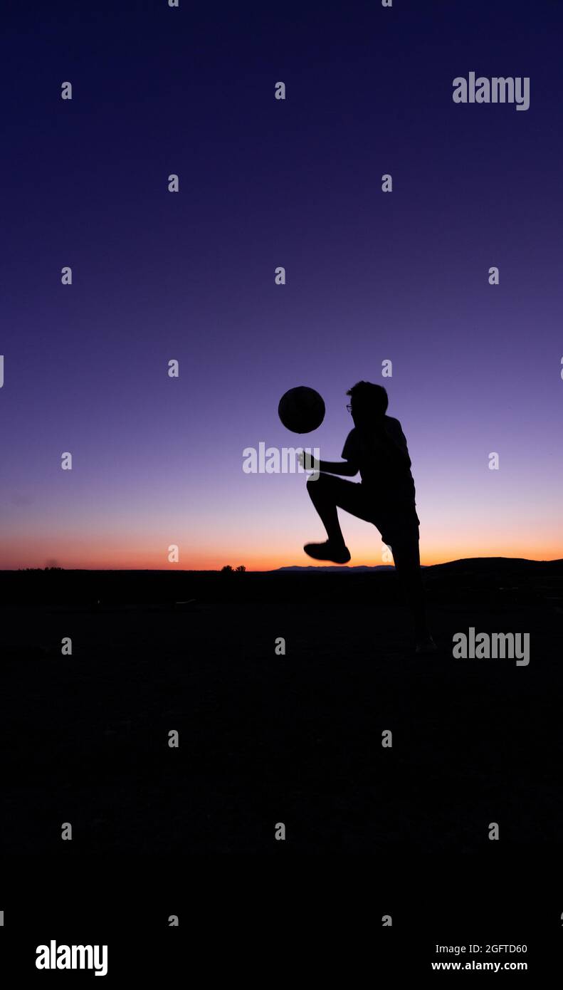 Vertical shot of a silhouette of a child jumping towards a ball during ...