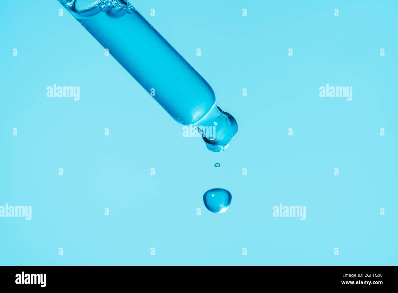 A drop of serum from a pipette. On a bright blue background. Front view ...