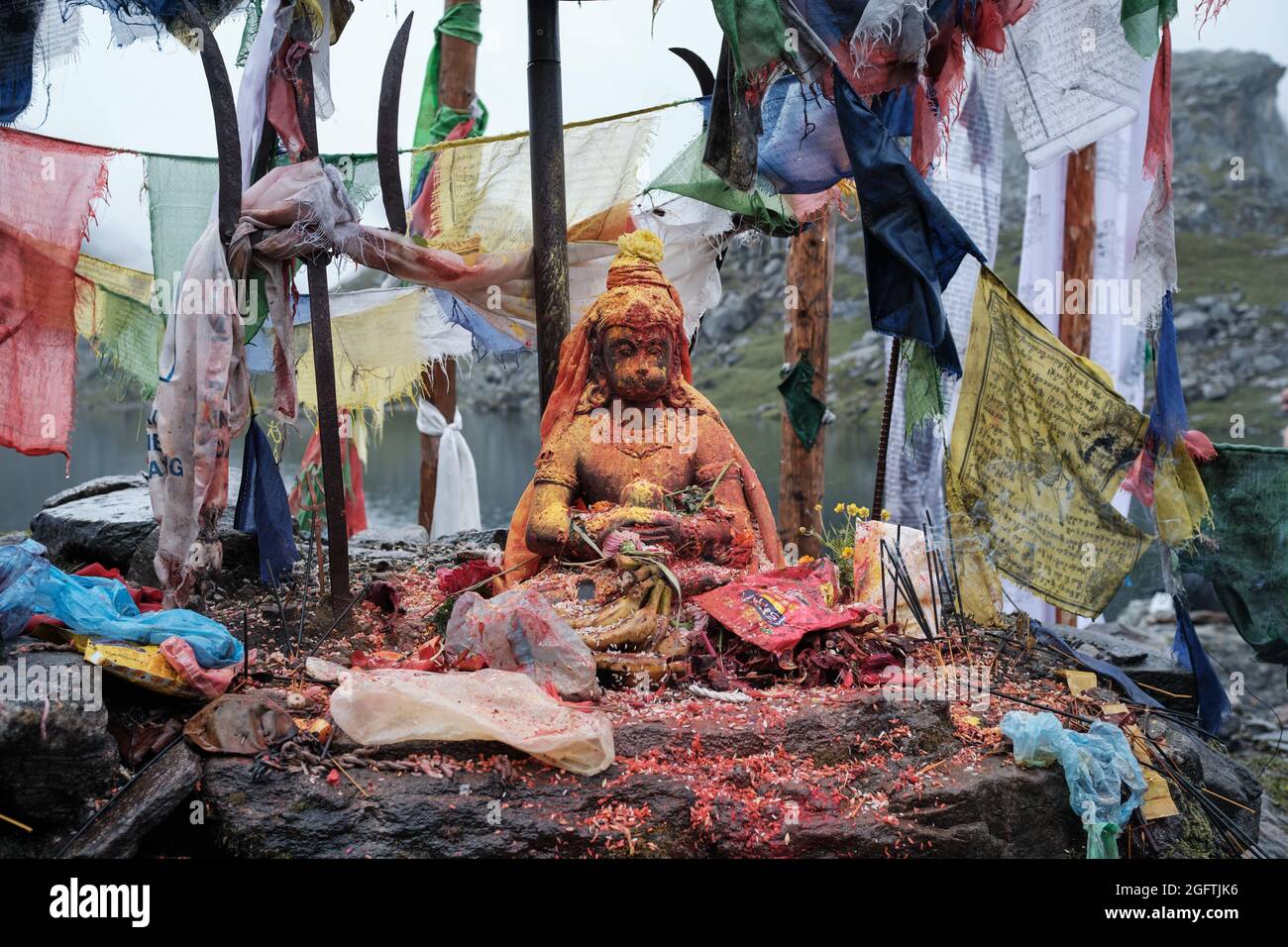 A Hindu idol surrounded by Buddhist prayer flags covered in colors ...