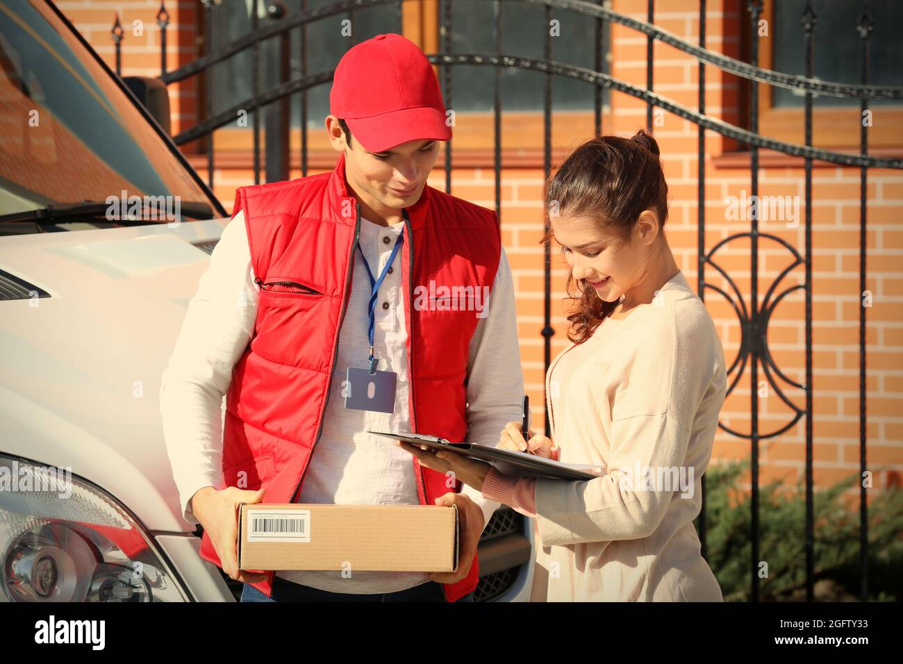 Young woman signing receipt for delivering parcel from male courier ...