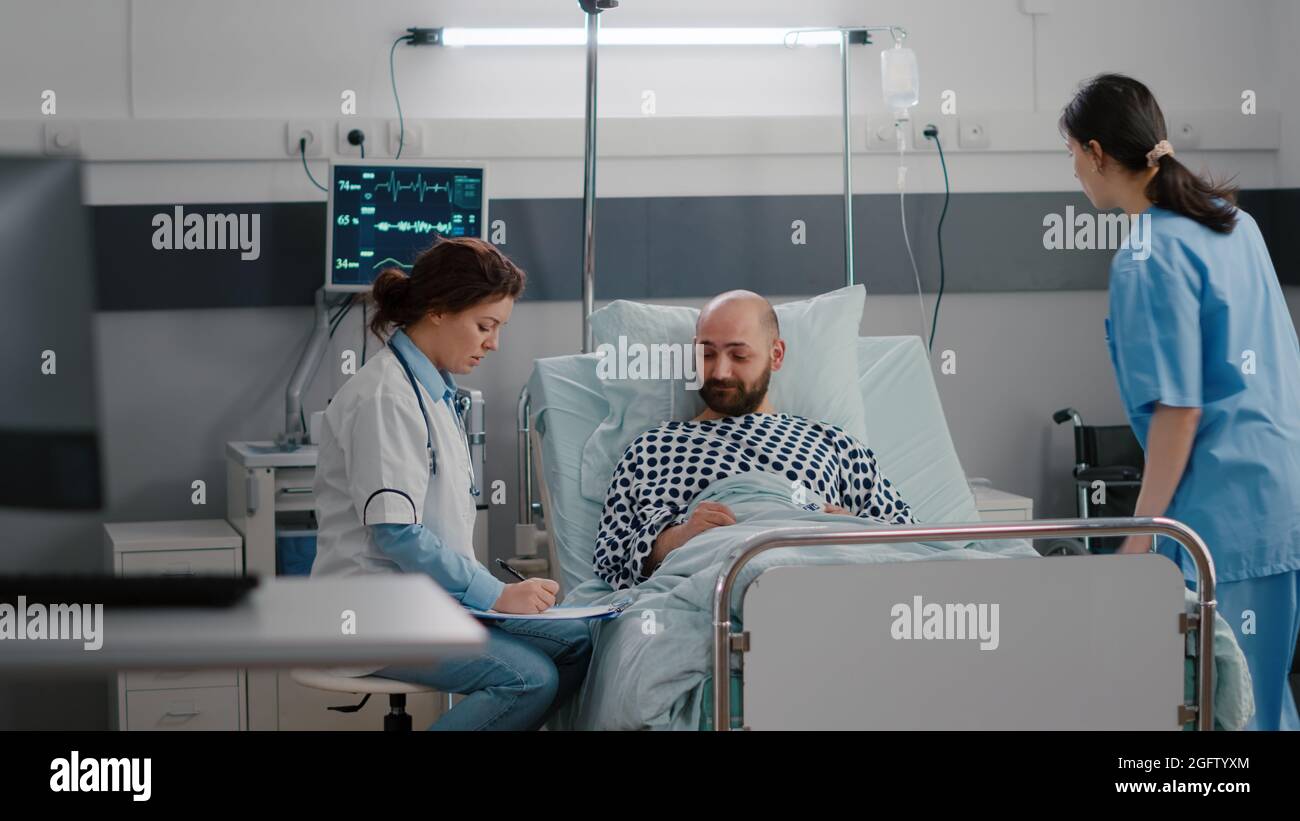 Black nurse checking patient vitals monitoring heart rate injecting vitamin in iv fluids drip ...