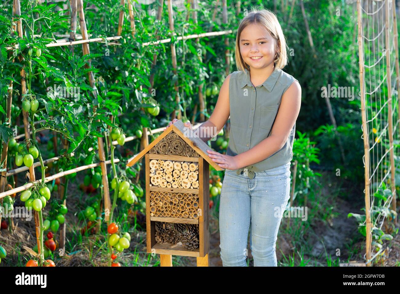 Portrait of happy girl next to hotel for insects in of wooden birdhouse ...