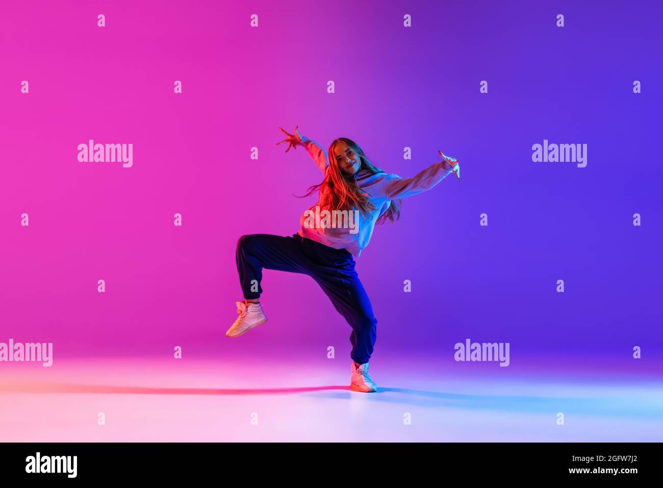 Attractive young girl dancing hip-hop isolated on gradient pink purple ...