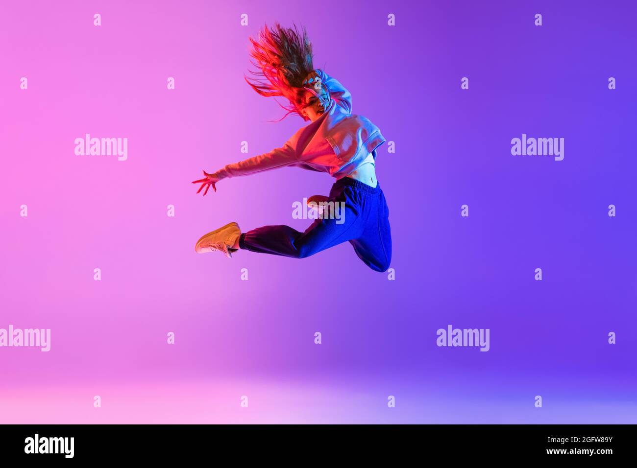In jump. Young stylish girl dancing hip-hop isolated on gradient pink ...