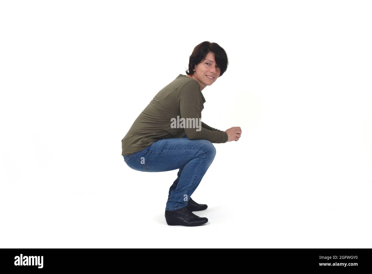 side view of a woman sitting squatting and looking at camera on white ...