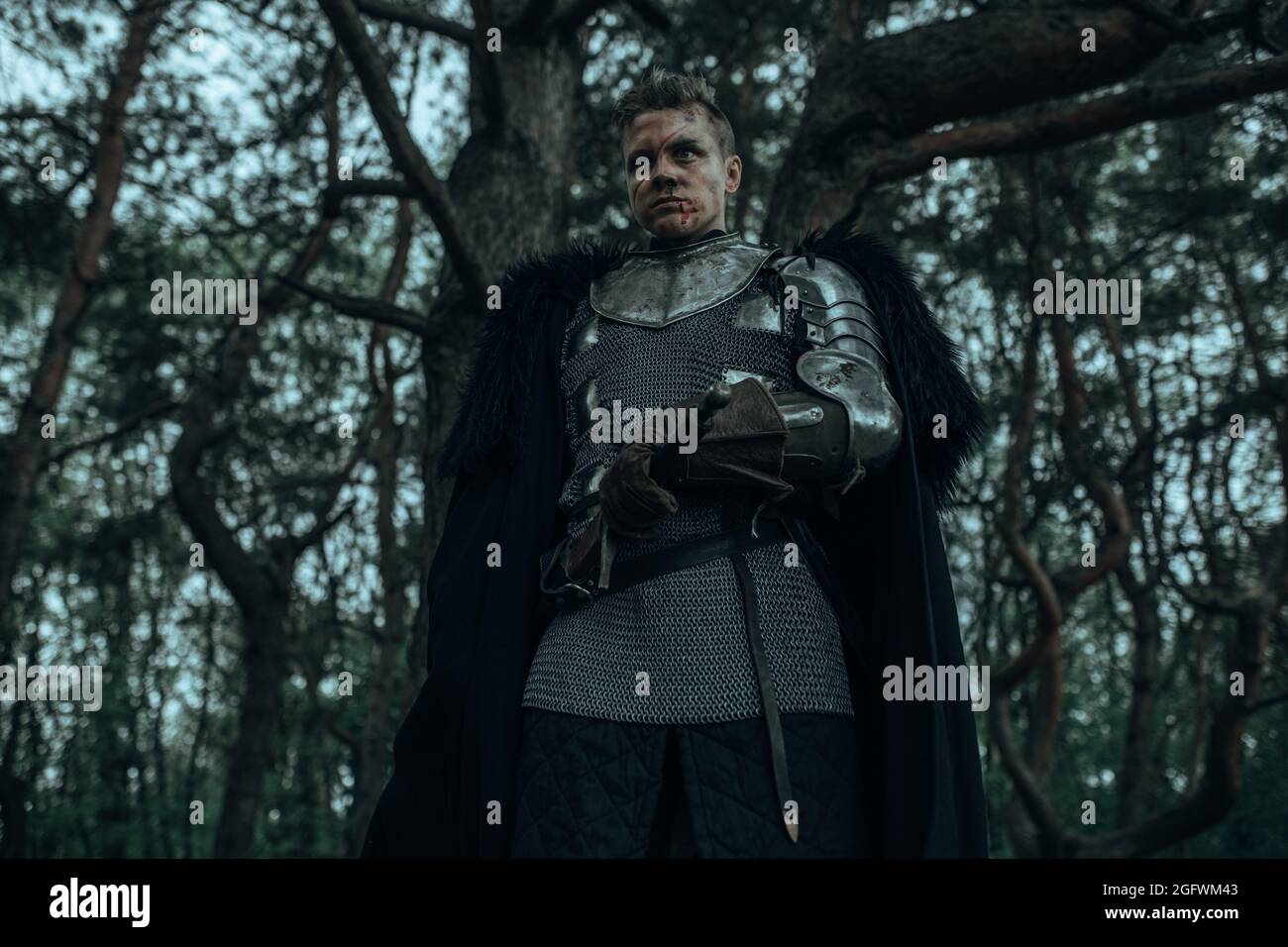 Medieval warrior knight in chain mail armour and black cape stands ...