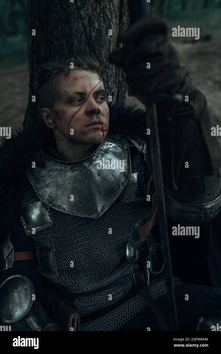 Medieval tired warrior knight in chain mail armour sits and rests among ...