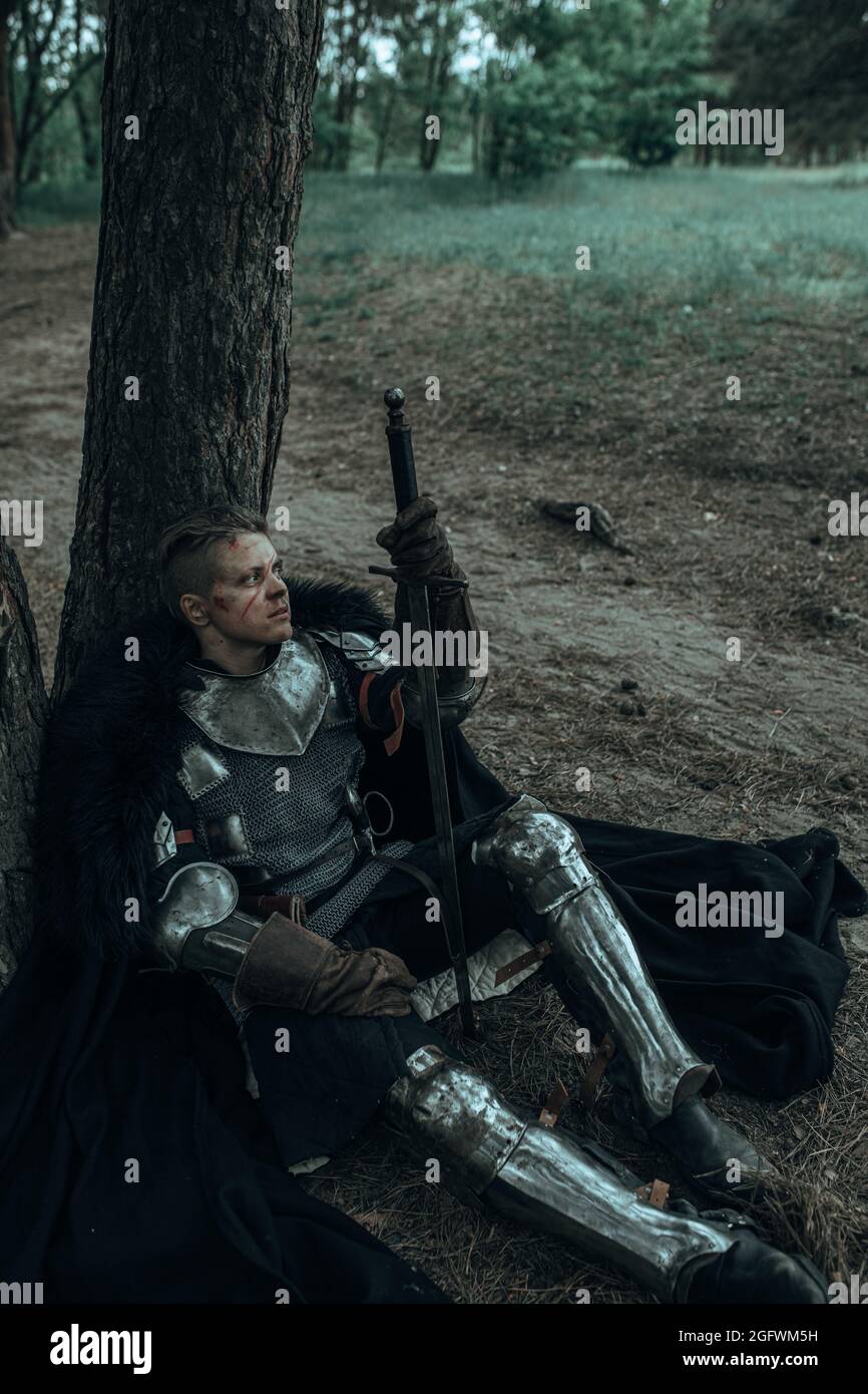 Medieval tired warrior knight in chain mail armour and black cape sits ...