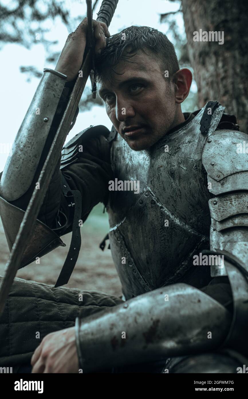 Medieval tired warrior knight in chain mail armour sits and rests among ...