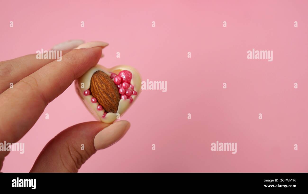 Hand holds white chocolate candies with almonds. Heart shaped sweets ...