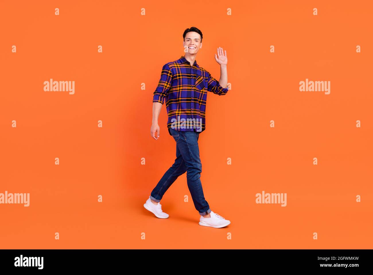 Full Body Profile Photo Of Young Cute Guy Go Wave Wear Shirt Jeans Sneakers Isolated On Orange 