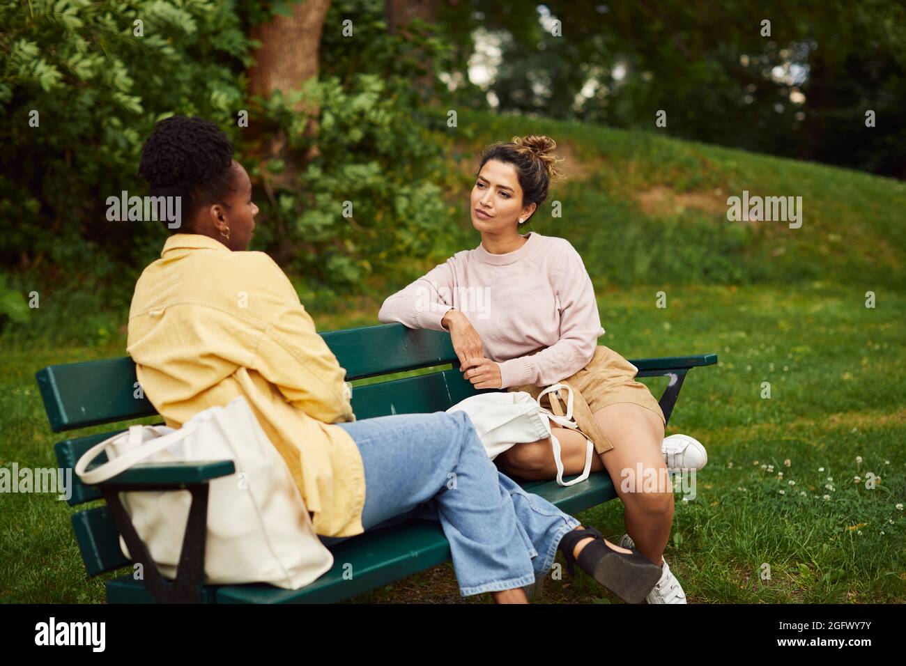 Female friends sitting on bench and talking Stock Photo - Alamy