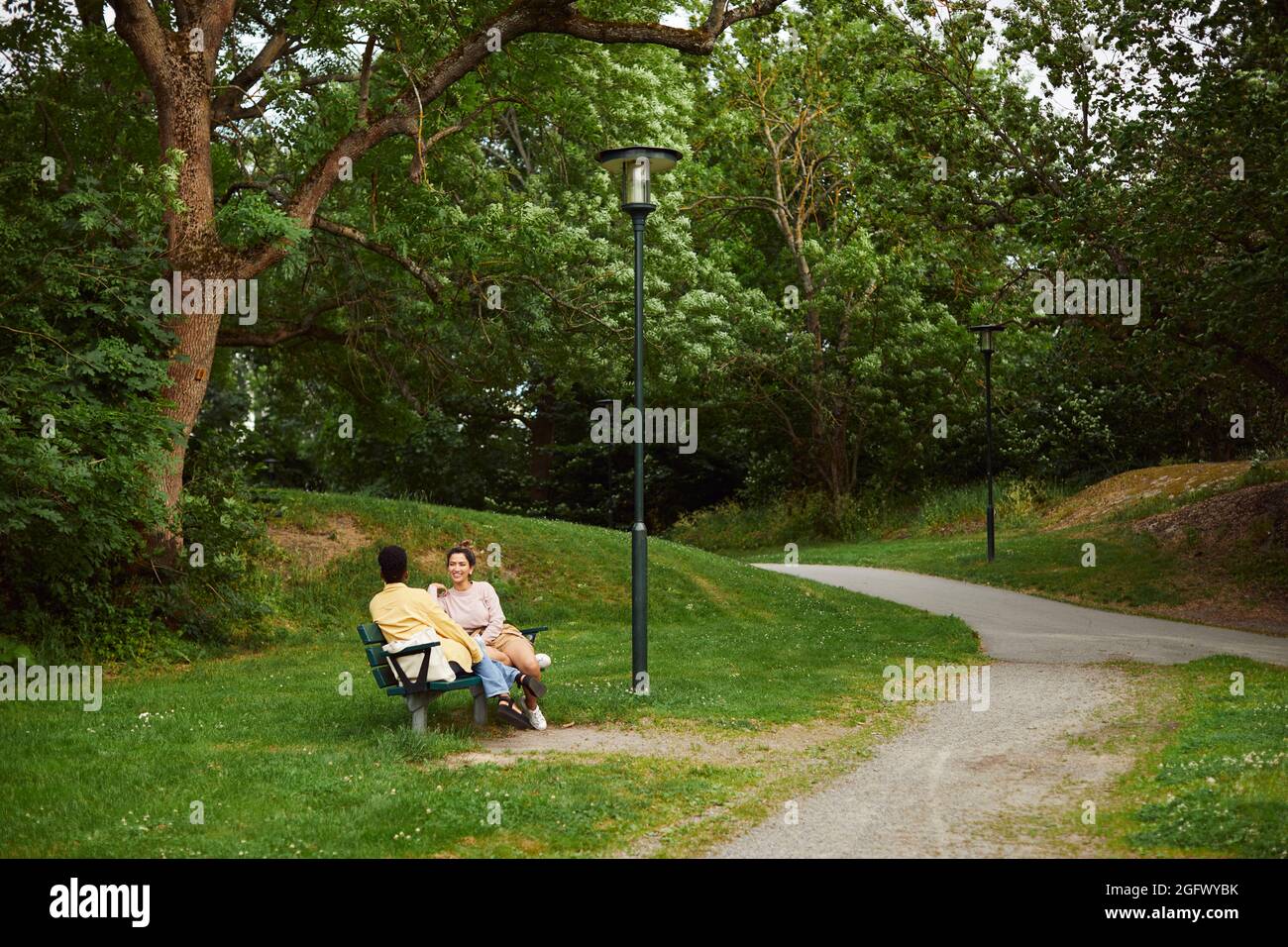 Female friends sitting on bench and talking Stock Photo - Alamy
