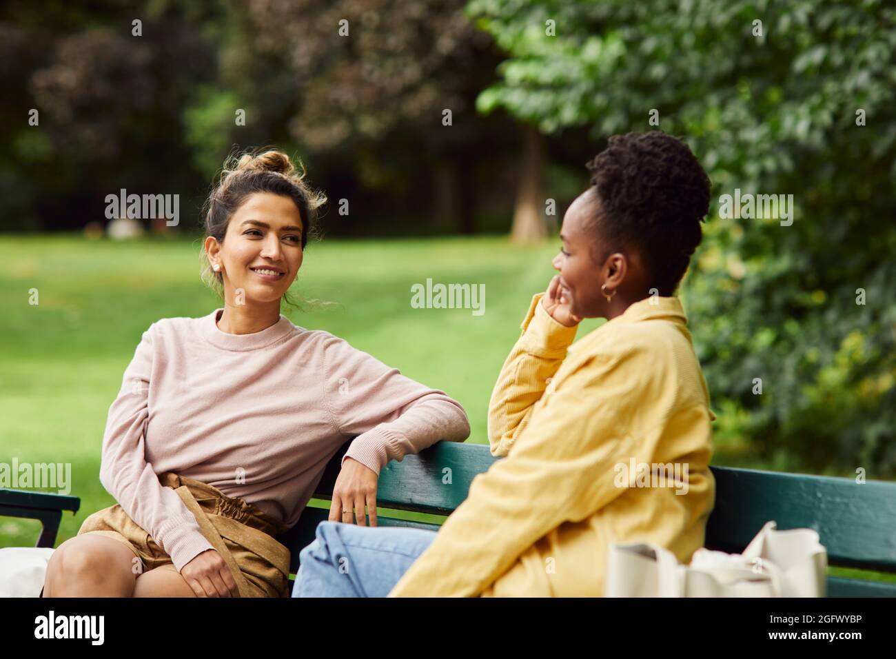 Female friends sitting on bench and talking Stock Photo - Alamy