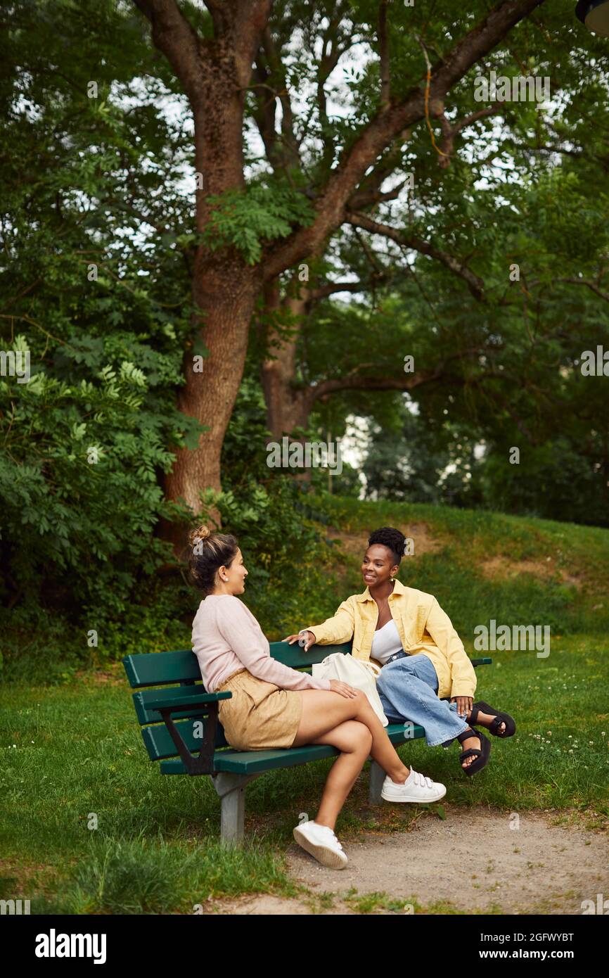 Female friends sitting on bench and talking Stock Photo - Alamy