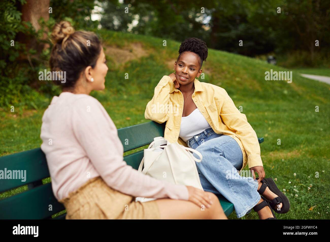 Female friends sitting on bench and talking Stock Photo - Alamy