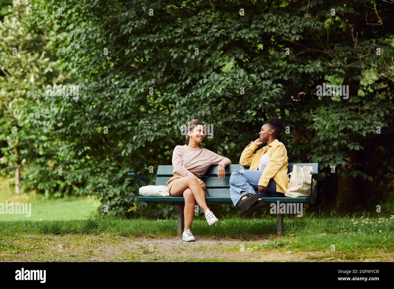 Female friends sitting on bench and talking Stock Photo - Alamy
